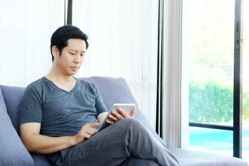 Asian Man Sitting on Sofa and Using Tablet Computer at Home, Lifestyle ...