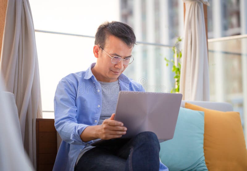 Asian Man Using Laptop Sitting on Sofa at Home, Man Working from a ...