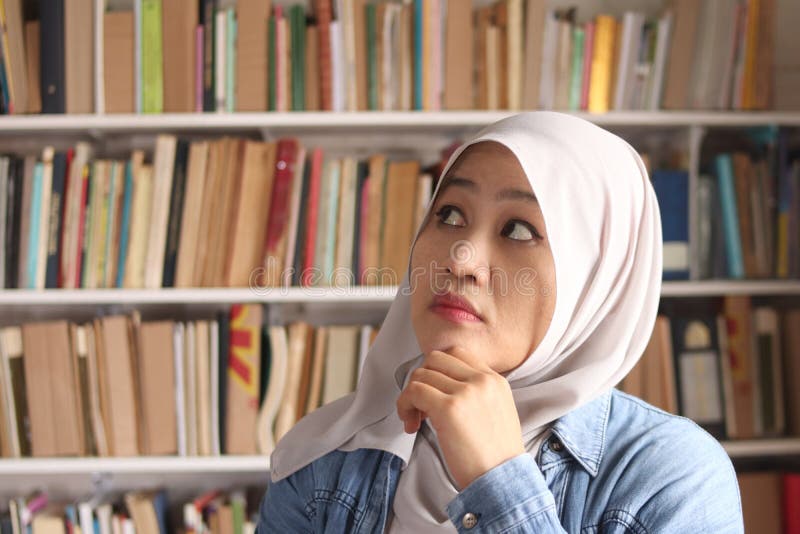 Asian Muslim Woman Thinking while Standing in Front of Bookshelf ...