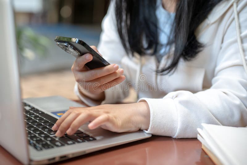 An Asian Woman is Multitasking, Working Remotely at a Cafe, Using Her ...