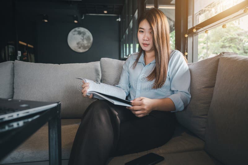 Asian Woman Sitting on a Sofa Reading a Book Inside a Cafe Stock Photo ...