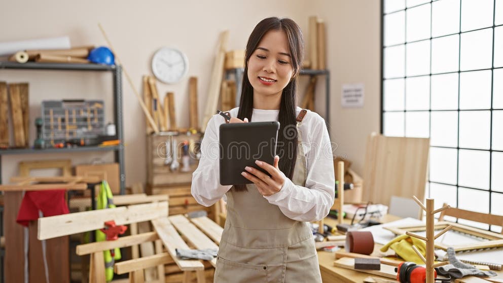 Asian Woman Using Tablet in a Woodworking Workshop Full of Tools and ...