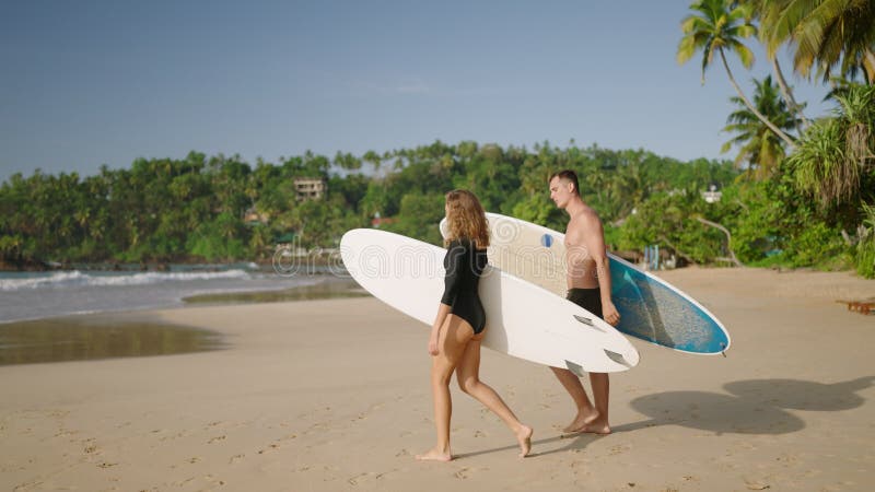 Romantic Couple With Surfboards Walking Towards Ocean Waves Among Green