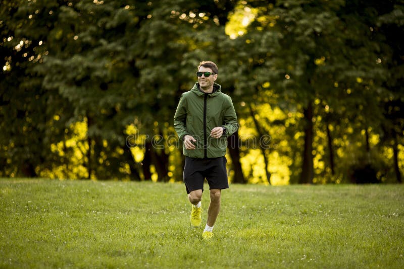 Athletic Young Man Running while Doing Workout in Sunny Green Park ...