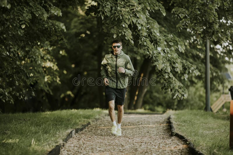 Athletic Young Man Running while Doing Workout in Sunny Green Park ...