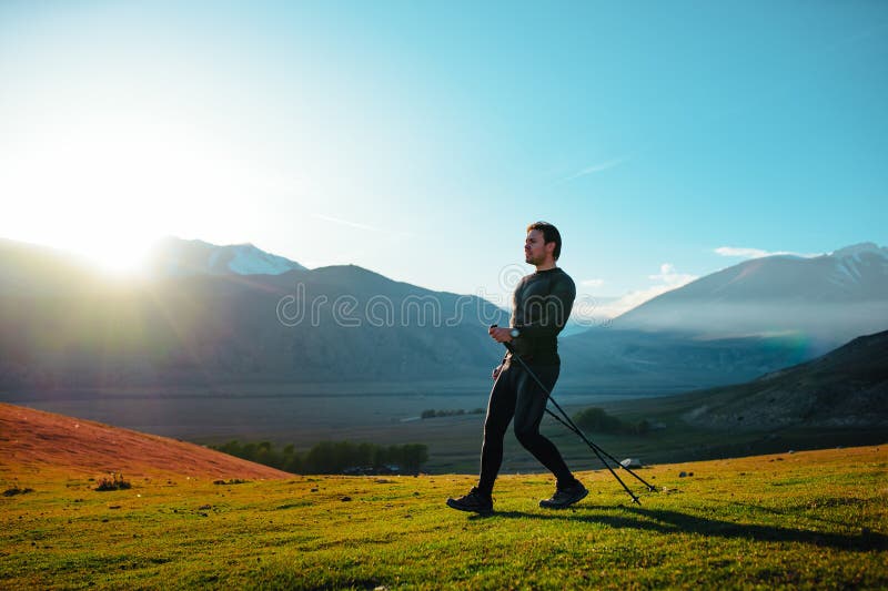 Athletic Man with Trekking Poles Walking on Mountains Background at ...