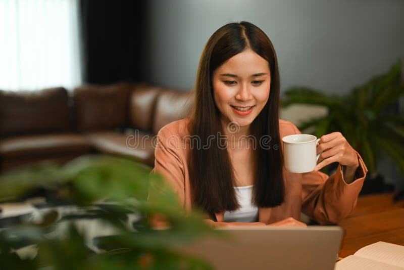 Attractive Asian Woman Drinking Coffee and Checking Email on Her Laptop ...