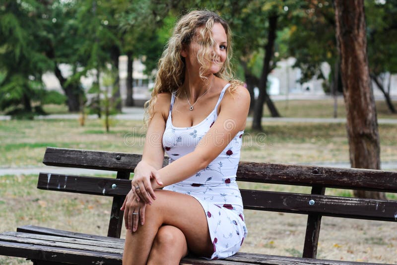 Attractive Blonde Girl With Curly Hair Sitting On The Bench In A Stock