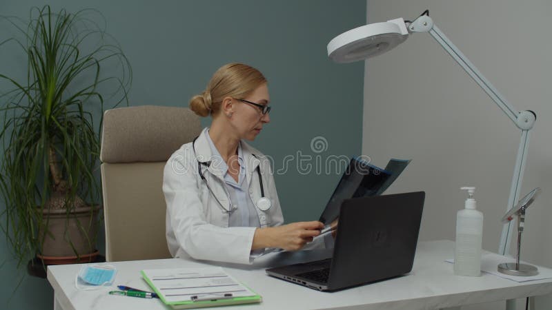Female Doctor Looking at X-ray Images, Taking Notes in Notepad Indoors ...