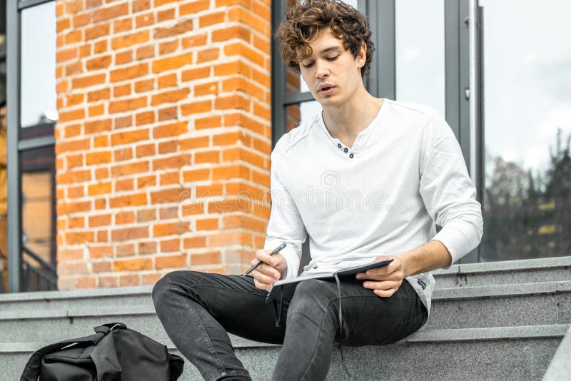 Attractive Man Holding Notepad in His Hands and Sitting on Concrete ...