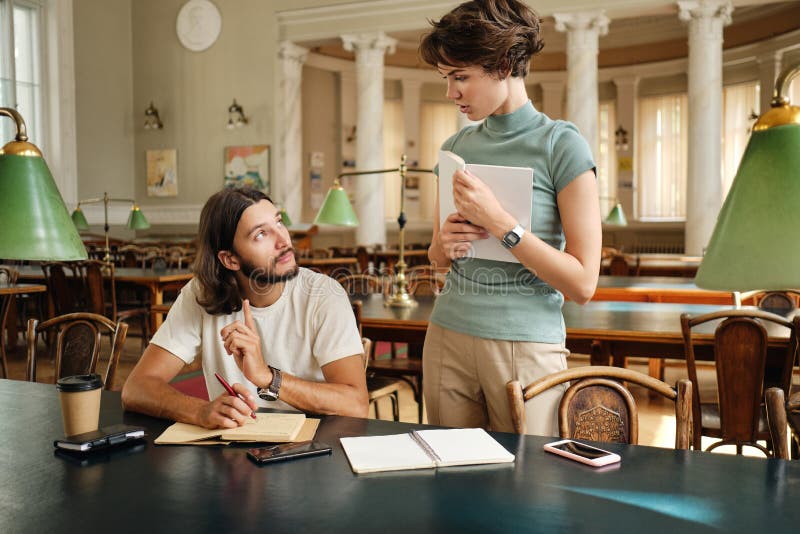 Attractive Tutor with Book Thoughtfully Discussing with Young Student ...