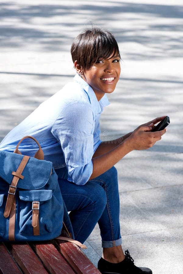 Smiling Young Woman Walking And Looking At Cell Phone Stock Image