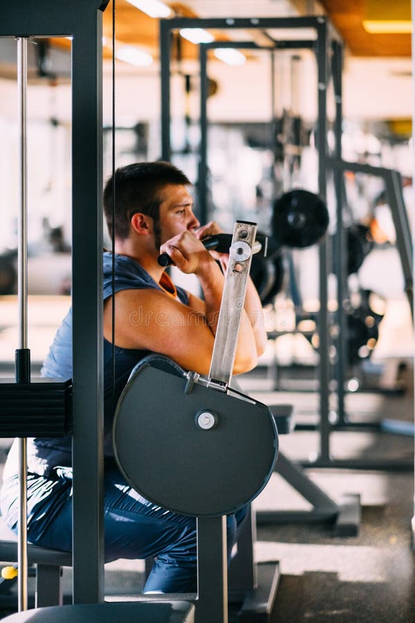 Attractive Young Man Doing Heavy Weight Exercise for Biceps on Machine ...