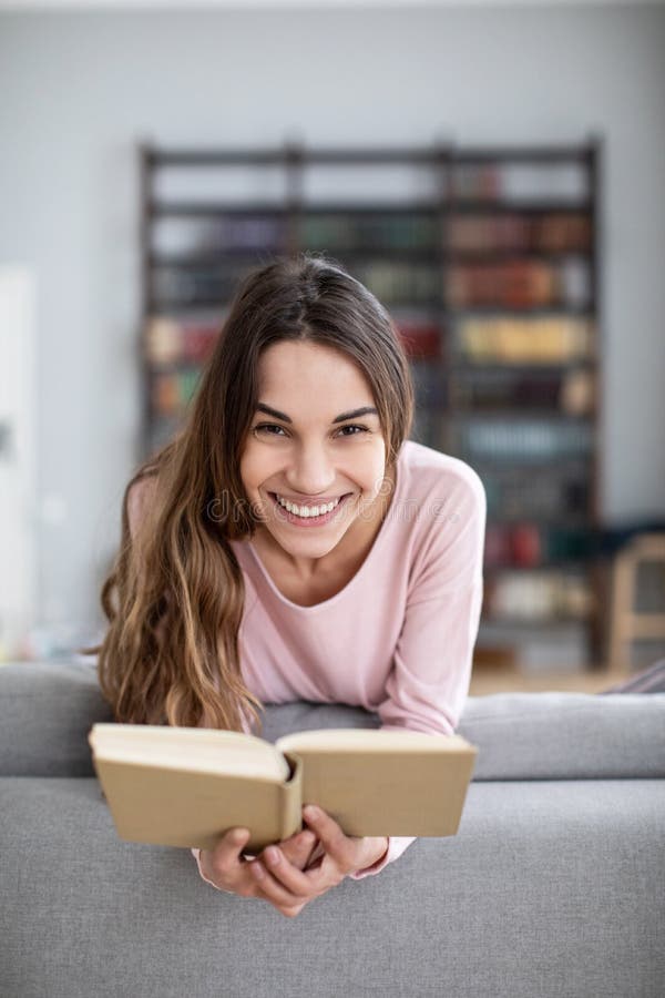 Attractive Young Woman is Reading a Book, Looking at Camera and Smiling ...