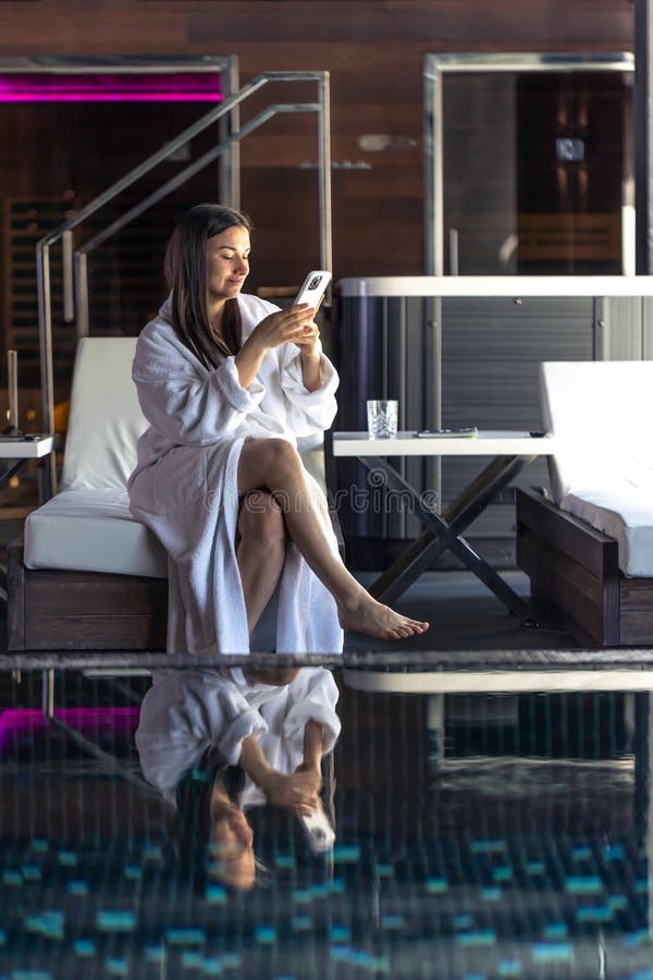 A Young Woman is Relaxing in a Spa Complex and Using a Smartphone ...
