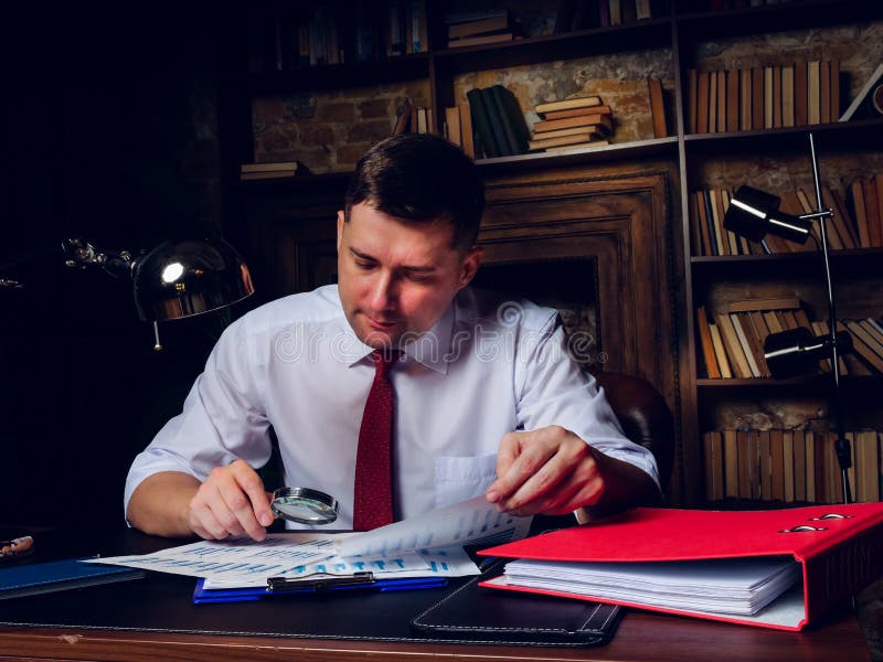 Man is Holding Magnifying Glass Above Business Documents with Financial ...