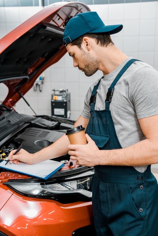 Auto Mechanic with Disposable Cup of Coffee Making Notes at Automobile ...