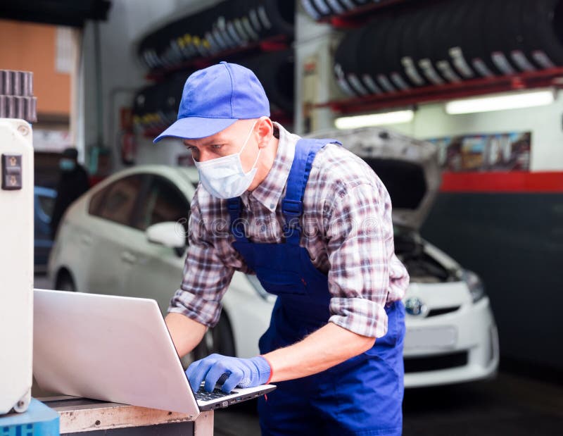Auto Mechanic in Face Mask Using a Laptop Computer Checking Car Stock ...
