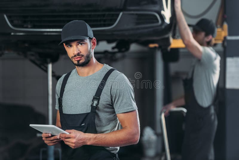Auto Mechanic in Overalls Using Digital Tablet while Colleague Working ...