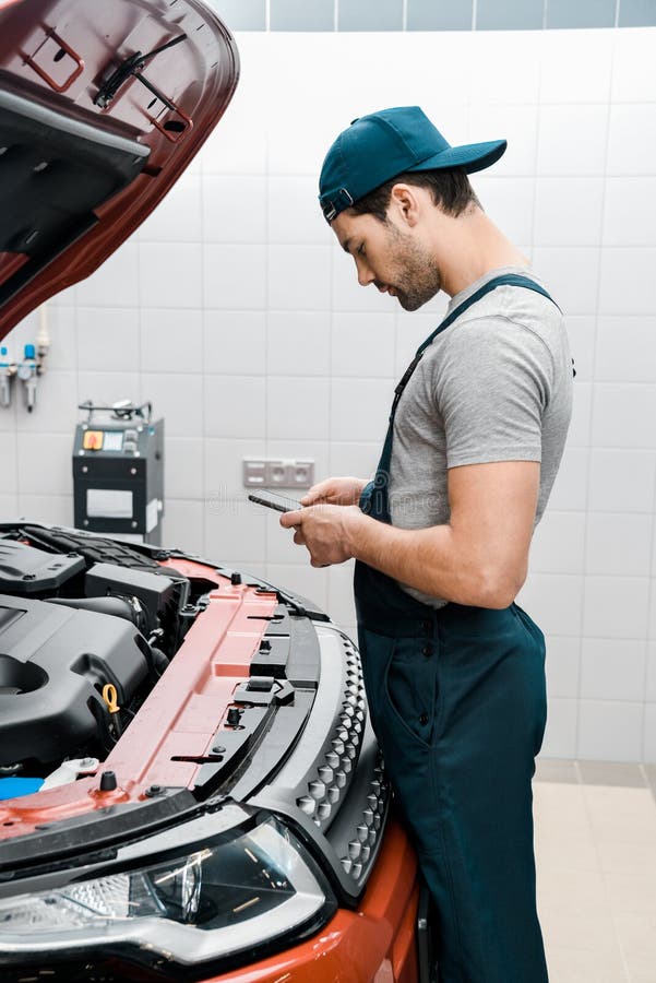 Auto Mechanic in Uniform Using Smartphone at Car with Opened Cowl Stock ...
