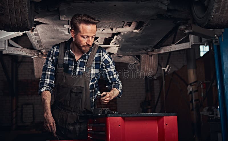 Auto Mechanic in a Uniform, Working on a Workbench while Standing Under ...