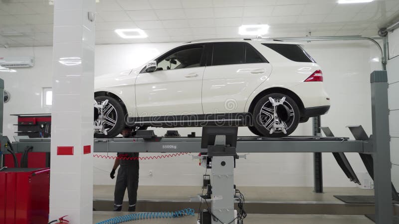 Auto Technician Aligns Wheels on Lift in Modern Garage. Vehicle ...