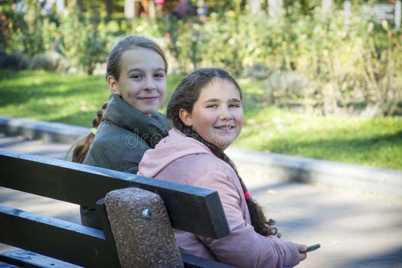 In Autumn, Two Girls Sit on a Bench in the Park Stock Photo - Image of ...