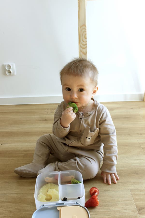 A Baby Boy Sits on the Floor and Eats Food from a Plastic Tray Stock ...