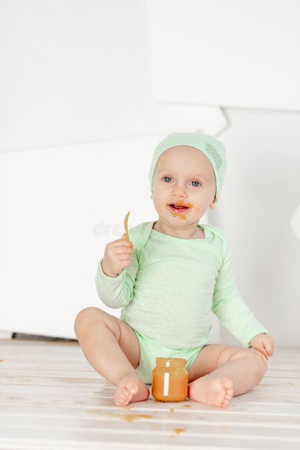 Baby Eats Fruit Puree with a Spoon in a Green Bodysuit, Feeding and ...