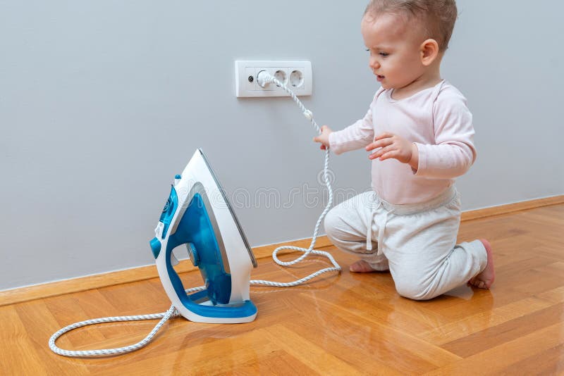 A Baby and an Iron Plugged into a Socket. Concept of Danger in the Home ...