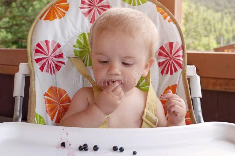 A Baby is Sitting in a Feeding Chair and Eating Blueberries Stock Image ...
