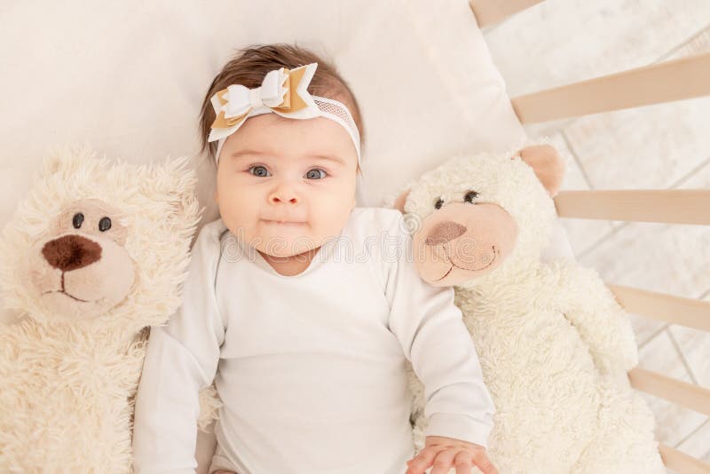 The Baby is Six Months Old in a Crib in a White Bodysuit with a Teddy ...