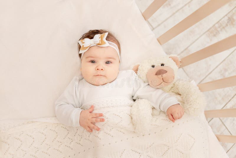 The Baby is Six Months Old in a Crib in a White Bodysuit with a Teddy ...