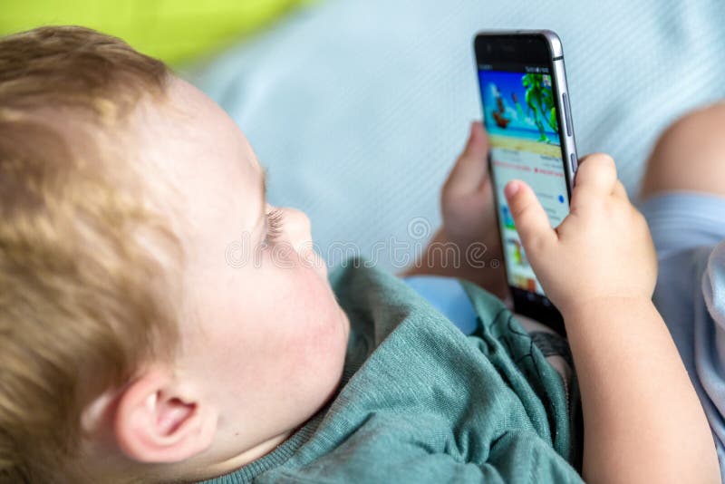 Small Baby Girl Lying on Bed and Looking on Smarthphone Screen at Night ...