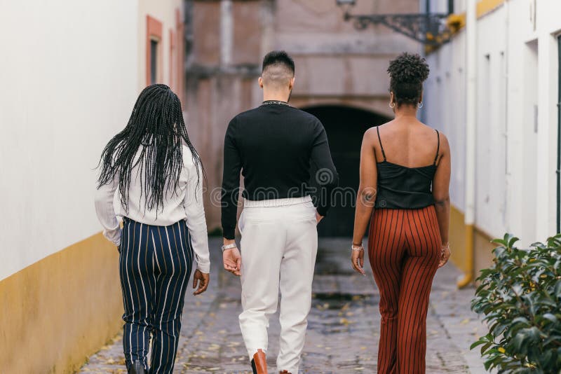 Back of a Man and Two Women in Modern Clothes Walking through a Street ...