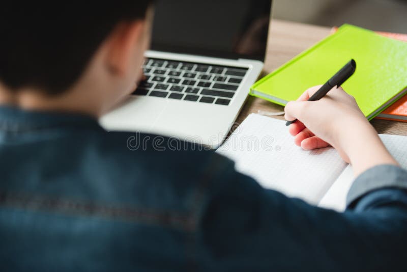 View of Boy Writing in Notebook and Using Laptop while Doing Homework ...