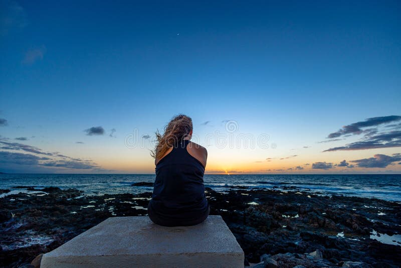 Back View of a Female Sitting on a Shore and Looking at Calm Sea during ...
