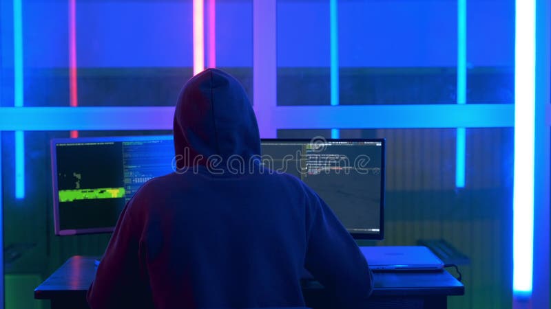 Back View of Hacker in a Black Jacket and a Hood on His Head, Writing ...