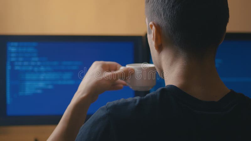 Back View Of Man Programmer Hacker Working And Drinking Coffee At Computer In The Data Center