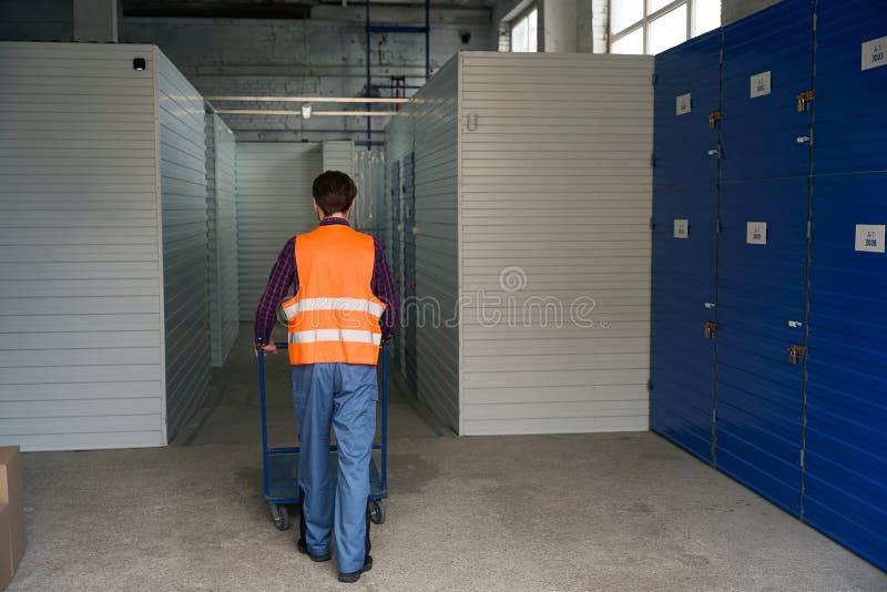 Back View of Man in Work Clothes with Platform Truck into Warehouse ...