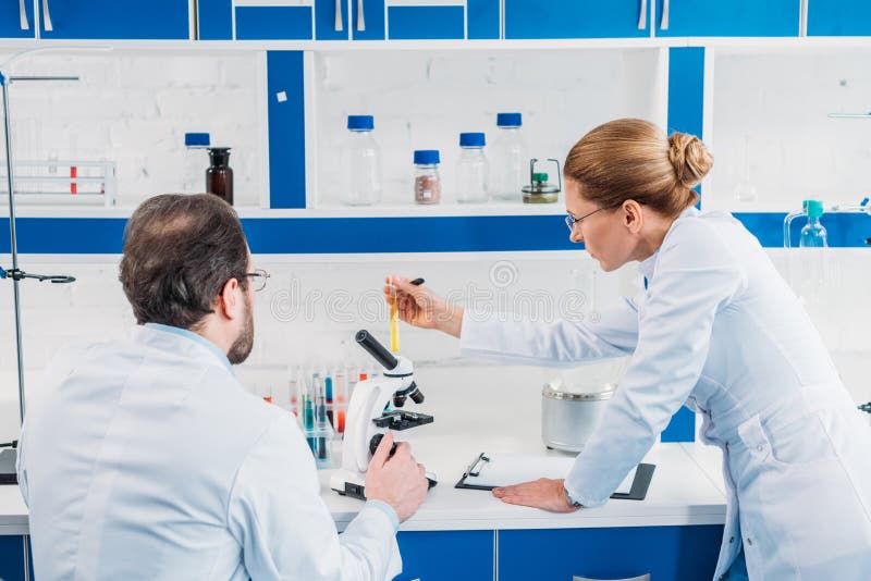 Back View of Scientists in White Coats Looking at Tube with Reagent ...