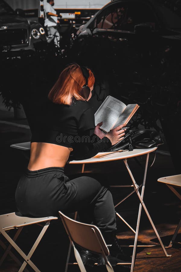 Back View of a Woman Sitting and Reading a Book while Wearing a Headset ...