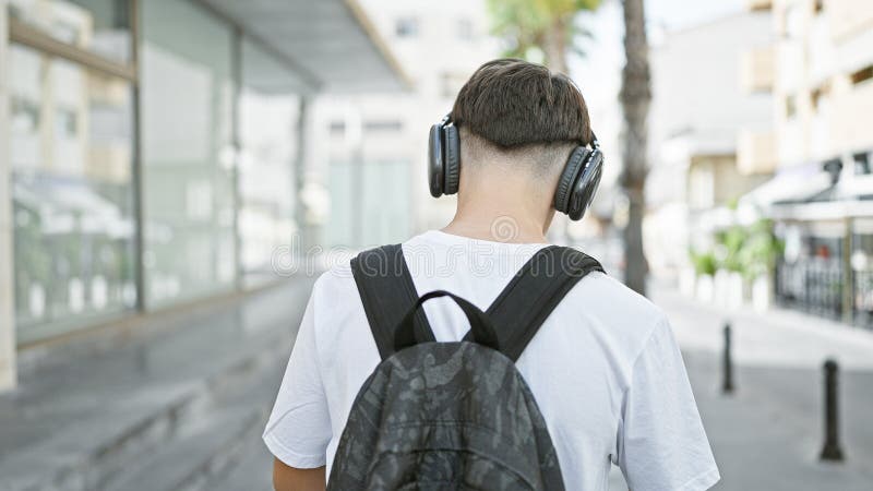 Back View of a Young Man with Headphones and a Backpack Walking in an ...