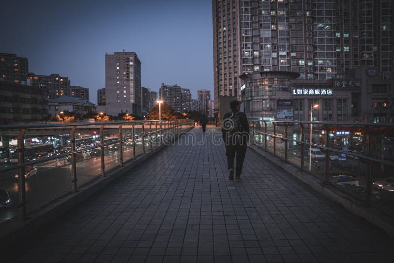 Back View of a Young Man Walking on a Bridge Above Busy Streets in the ...