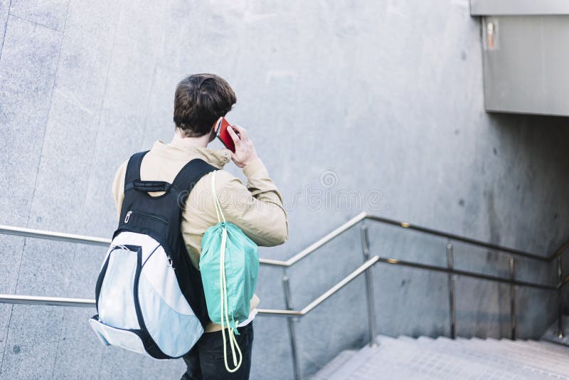 Back View of a Young Man Walking Down Stairs with Backpack while Using ...