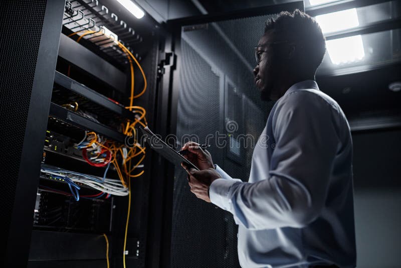 Backlit Black Man Working with Server Cabinet and Taking Notes on ...