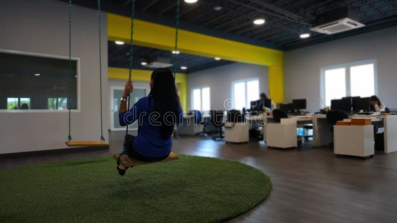 Backshot of a Young Woman Sitting on a Swing Inside the Office Stock ...