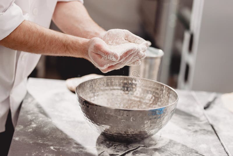 Baker Adds Flour To Dough in an Iron Bowl on the Table in the Bakery ...