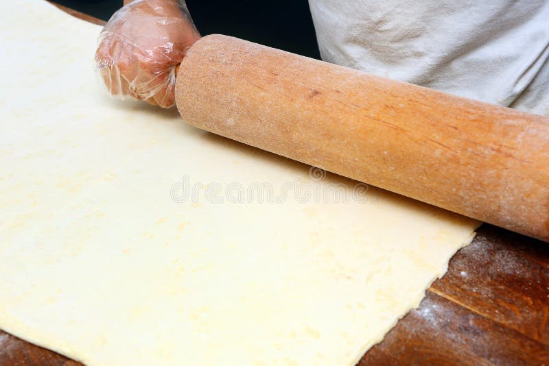 Baker Rolls Out the Dough on a Wooden Kitchen Table Sprinkled with ...