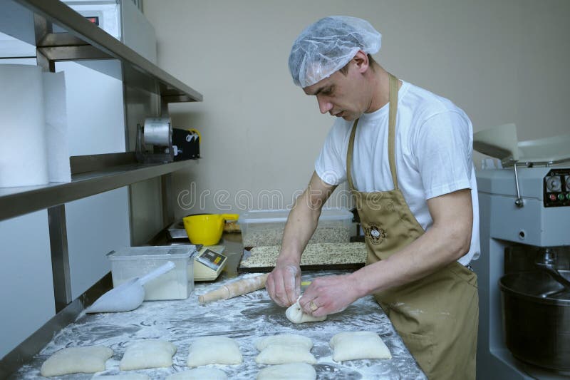 At the Bakery: Baker Standing at a Work Table and Molding Dough for ...
